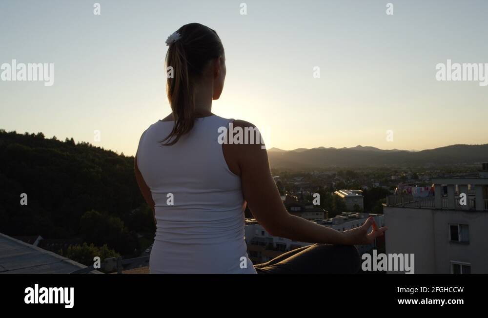 CLOSE UP: Yoga girl sitting on the edge on rooftop, meditating in lotus ...
