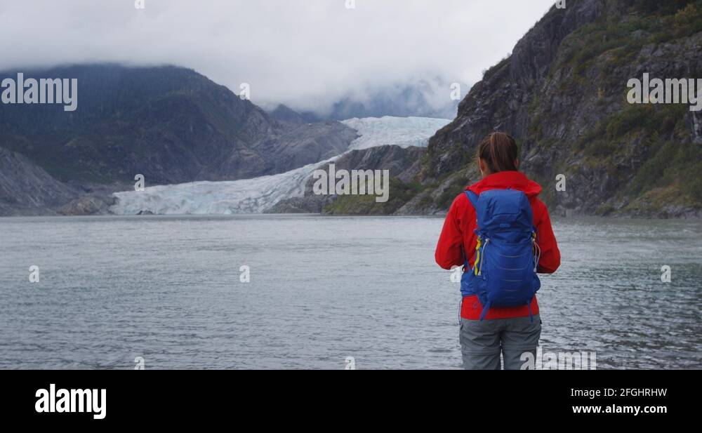Hiking woman wearing hiker backpack in Alaska looking at glacier ...