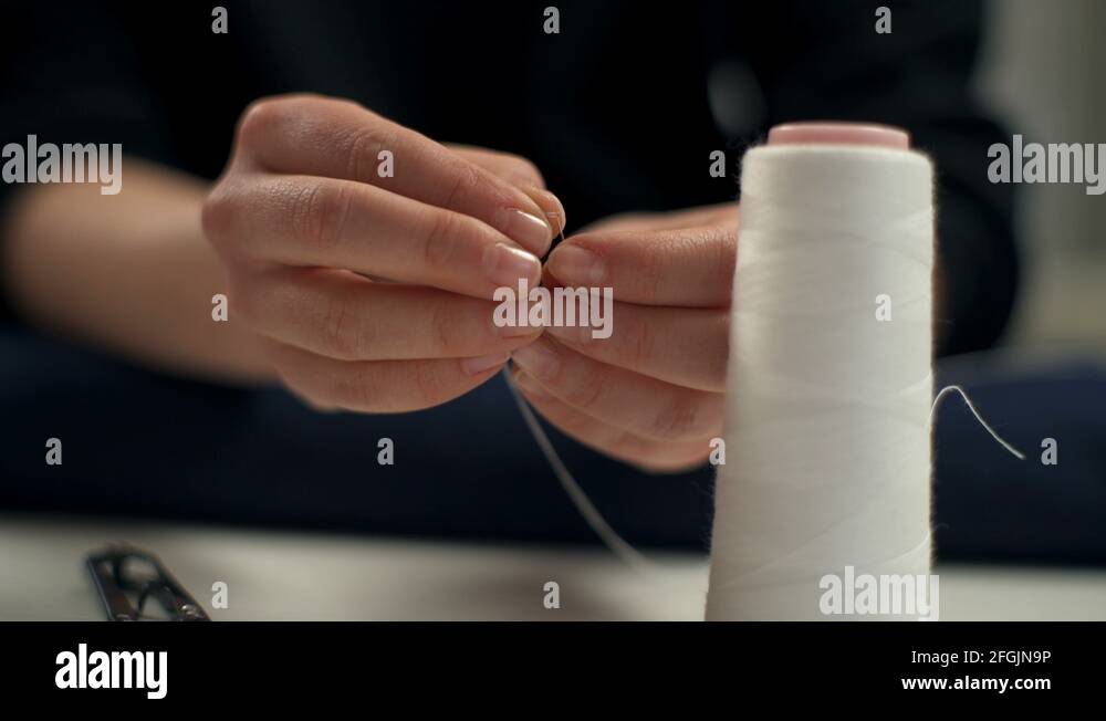 Seamstress threading the needle with folded in half white thread in the ...