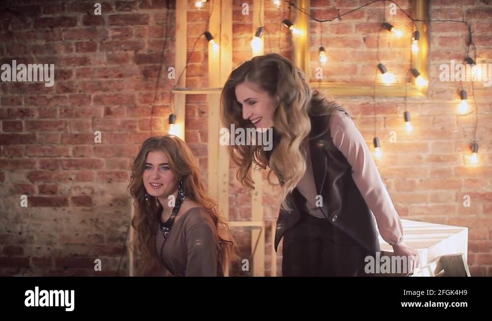 Two girls in the loft interior. Brick wall. Lamps, wooden frames and ...