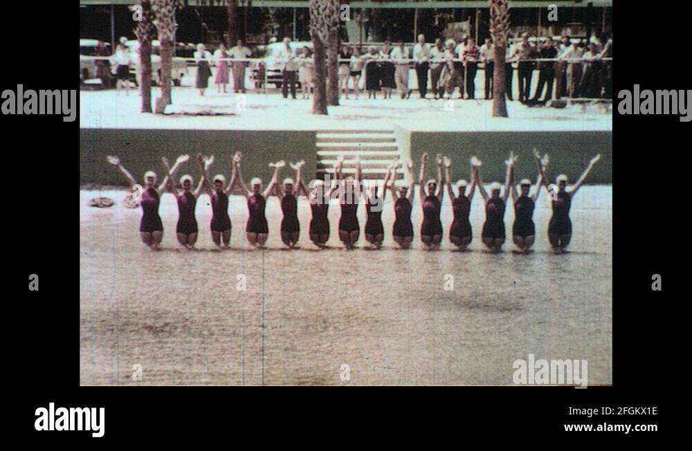 1960s: Synchronized swimmers dive in water, crowd in background / high ...