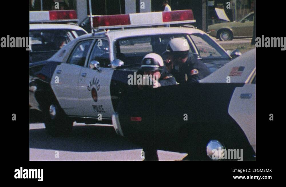 1970s: Police officer points gun behind car, zoom out, men on ground ...