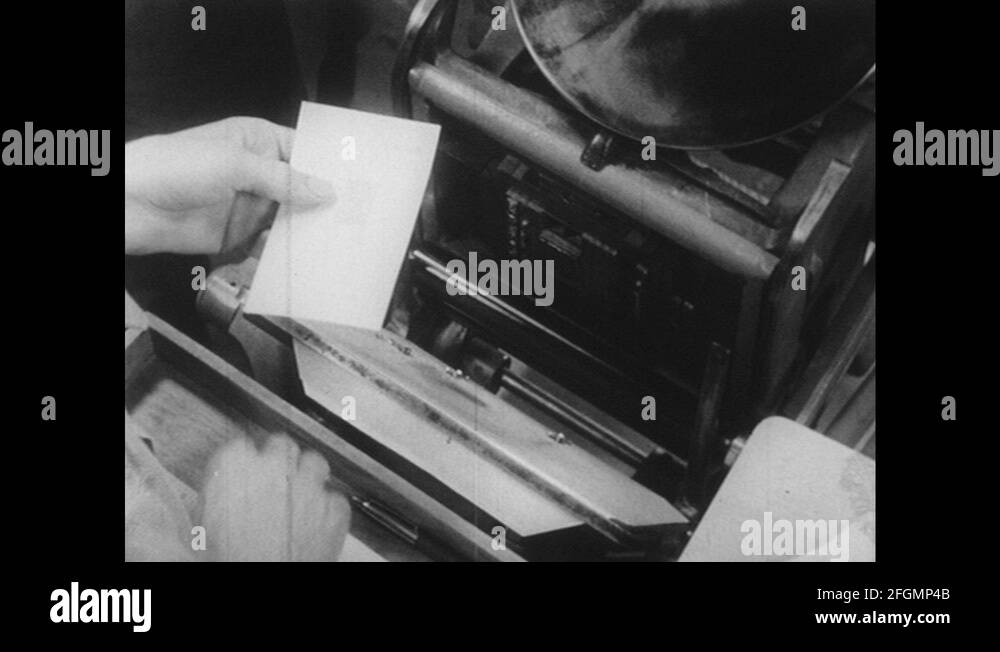 1950s: UNITED STATES: man checks alignment of paper in press. Boy ...