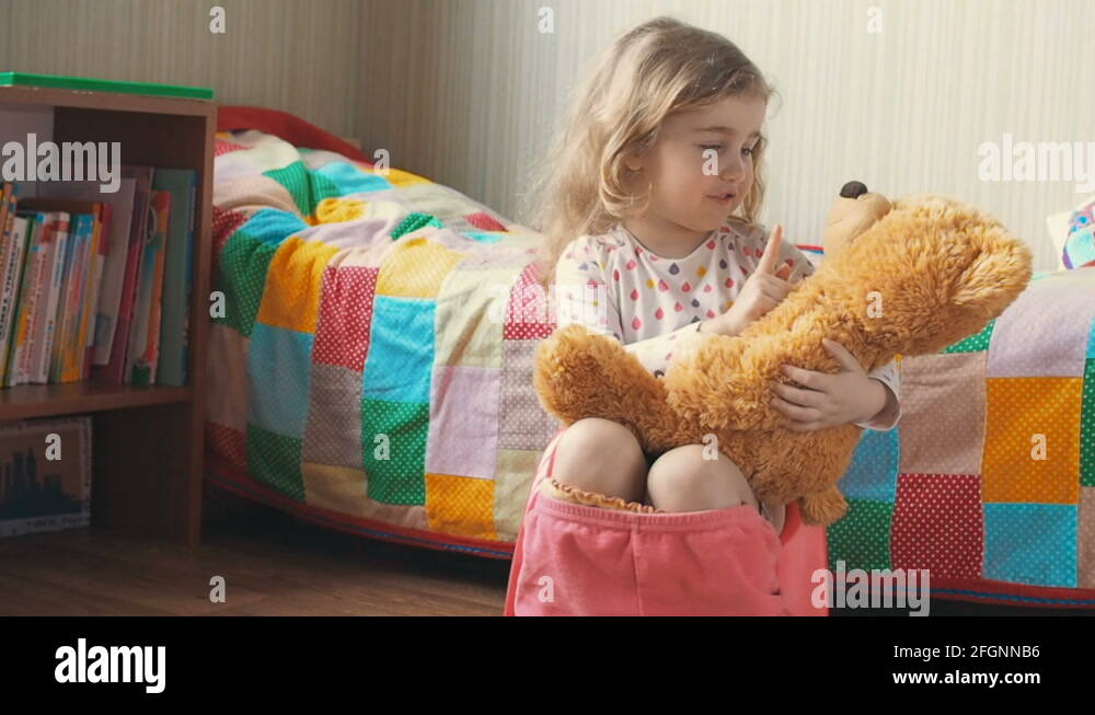 Little girl sitting on the potty beside the bed and plays with a Teddy ...