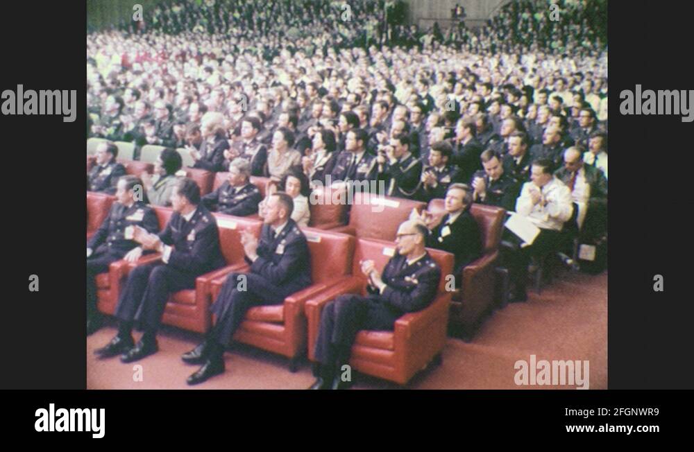 1970s: Audience clapping, seated. Line of men in uniform receive ...