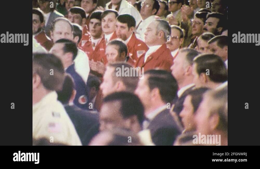 1970s: Audience members rise from seats, clap. Men in uniform clap on ...