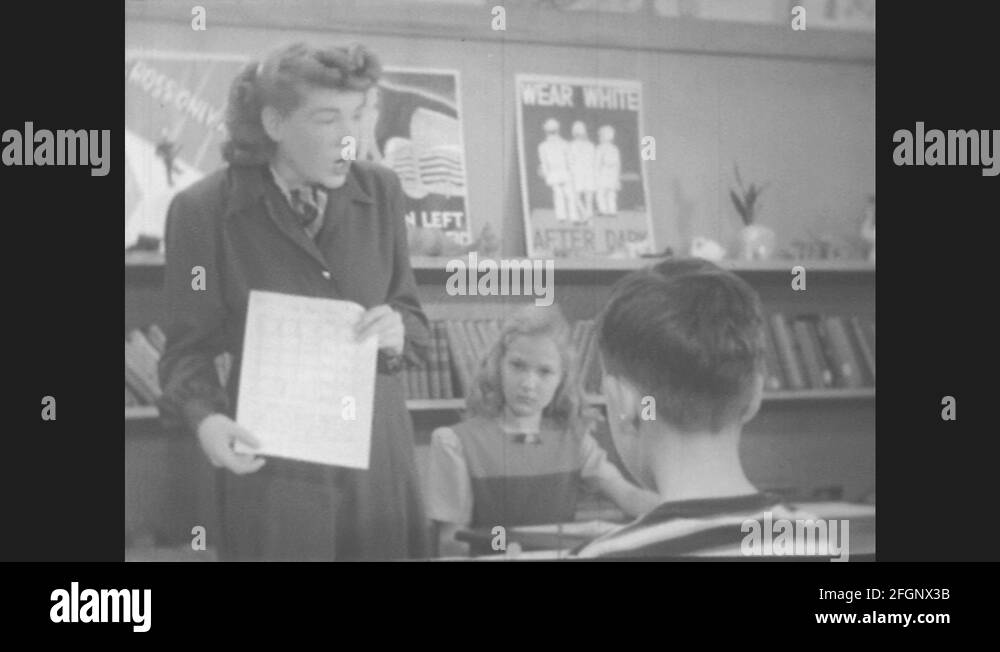 1940s: Teacher in classroom points to street map on paper. Teacher ...