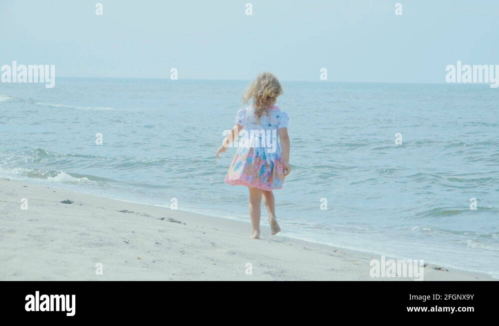 Adorable little girl in a dress runs jumping on the beach. Child enjoys ...