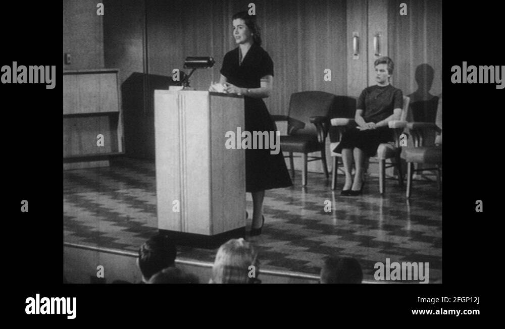 1950s: Young woman speaks and gestures at lectern. Woman puts down ...