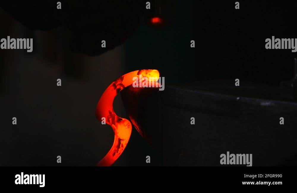 blacksmith working with hot glowing metal, bending steel in a smithery ...