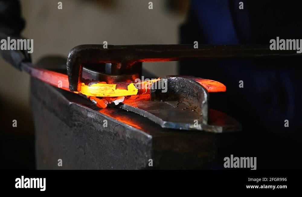 blacksmith working with hot glowing metal, bending steel in a smithery ...
