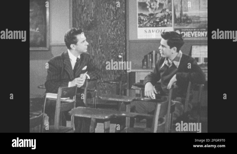 1950s: Teacher and teenage boy talk in classroom. Men smile and laugh ...
