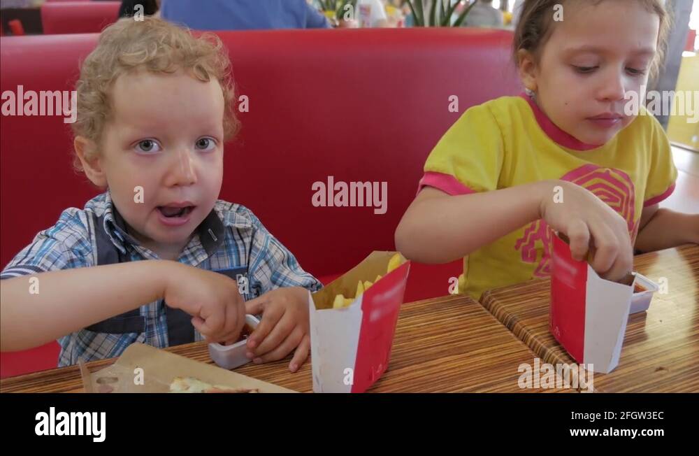 Little kid boy and girl close-up eating french fries in a fast food ...