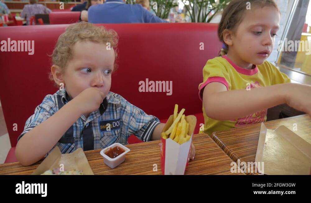 Little kid boy and girl close-up eating french fries in a fast food ...