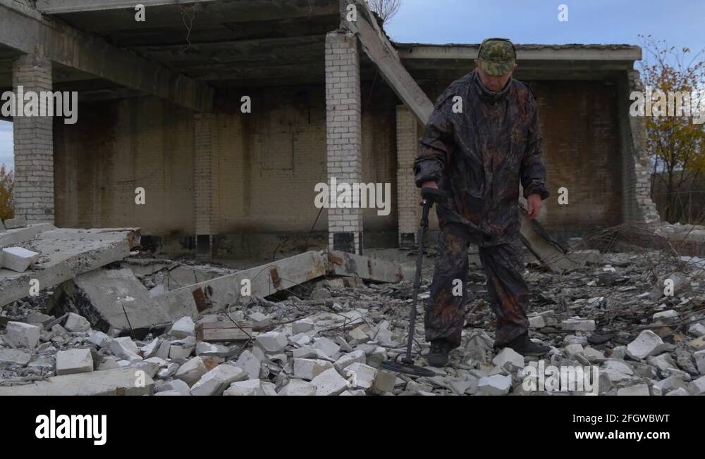 The soldier works with a mine detector in the ruins of houses in search ...