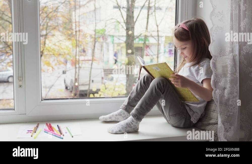 Little girl is sitting on a window sill and reading a book Stock Video ...