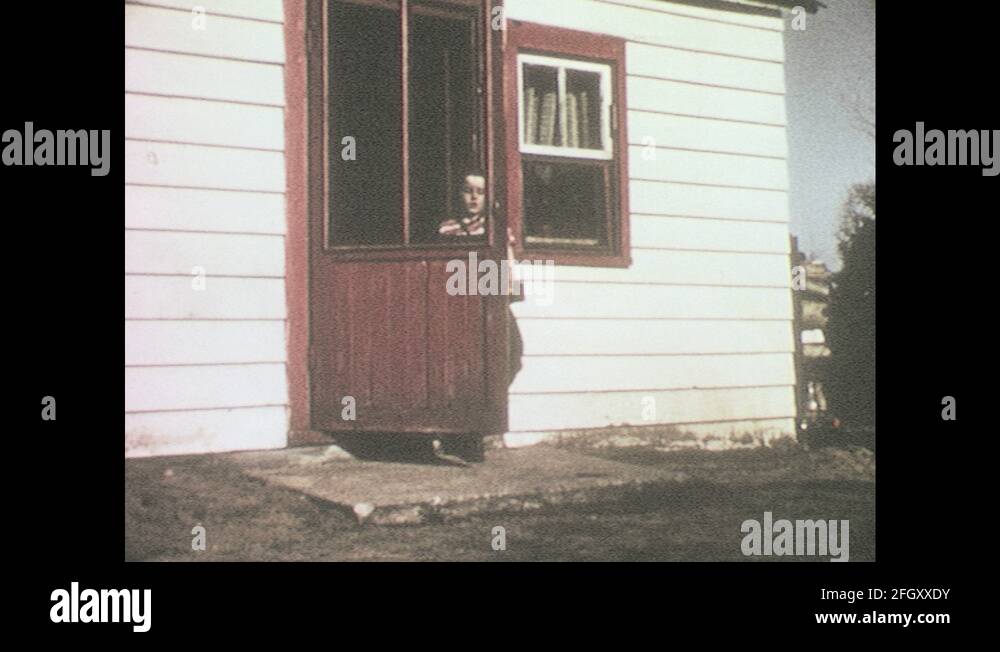 1950s: UNITED STATES: boy exits door. Boy carries young plants in box ...