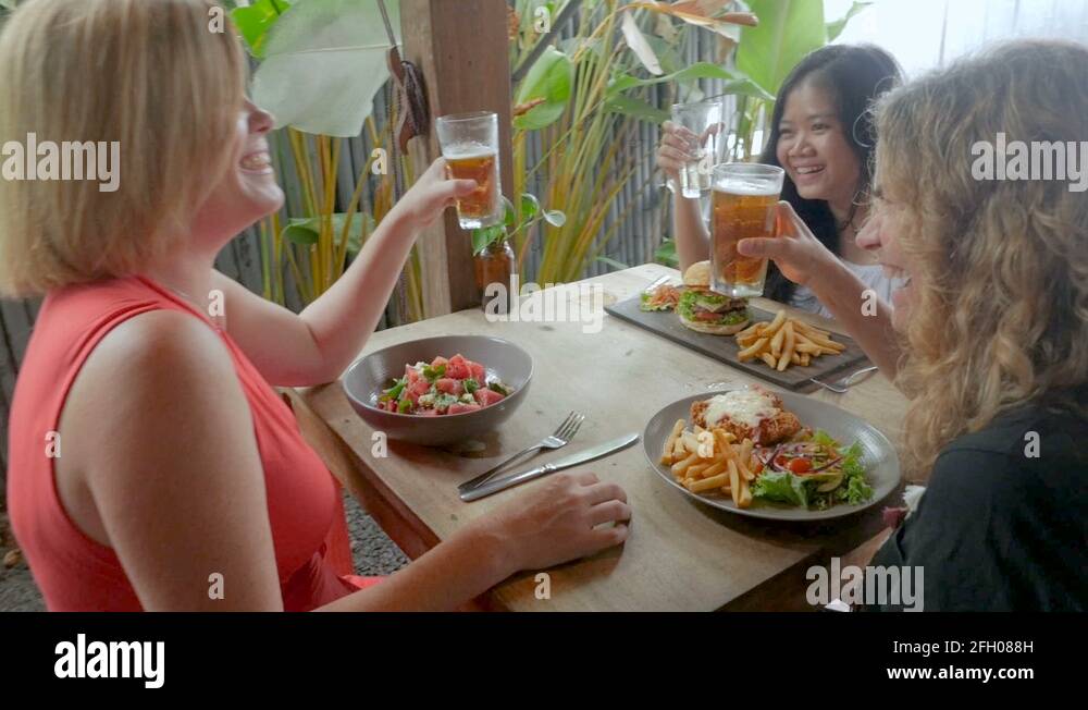 Three beautiful young women laughing and celebrating over a meal and ...