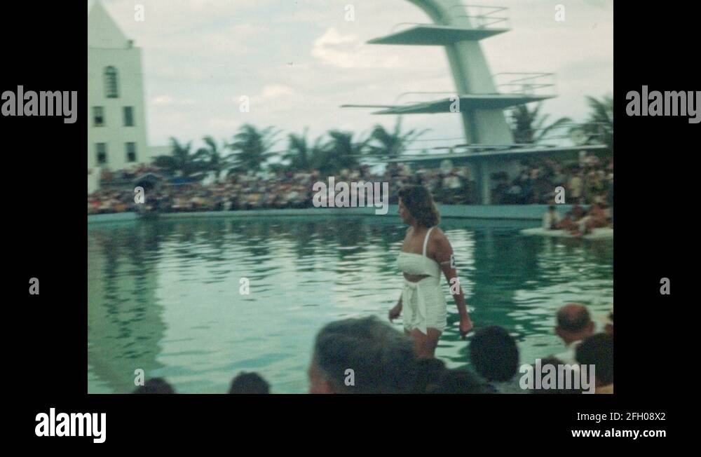 1940s: Large seated crowd at swimming pool, various women walk by in ...