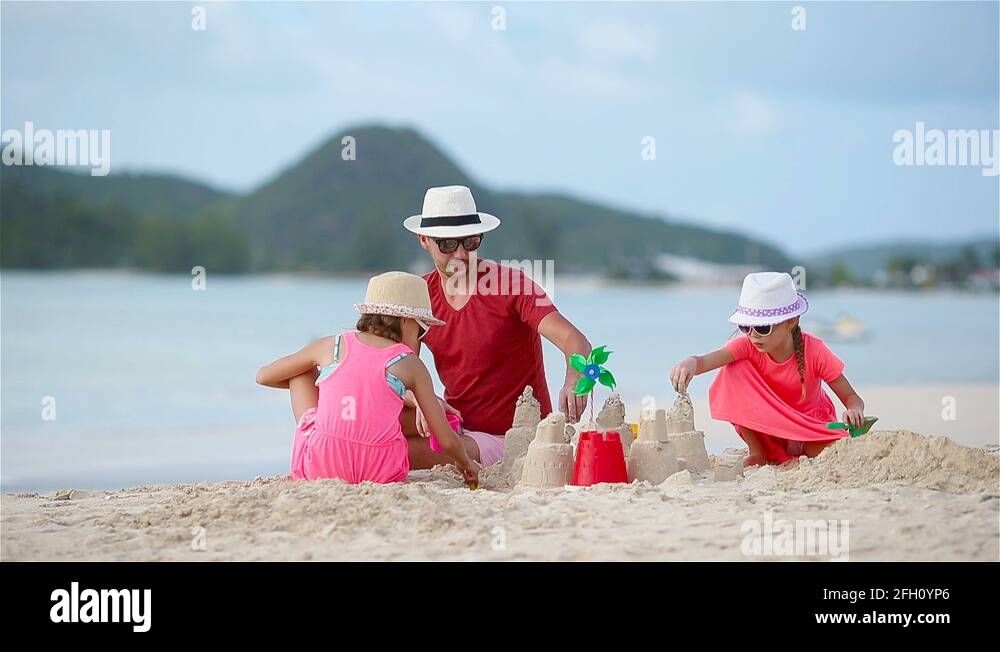 Father and two girls playing with sand and making sand castle on ...