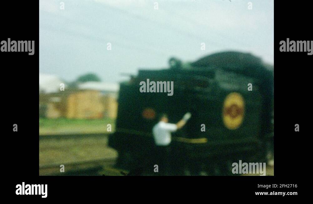 1940s: Conductor rides on back of train. Man peeks out window of train ...