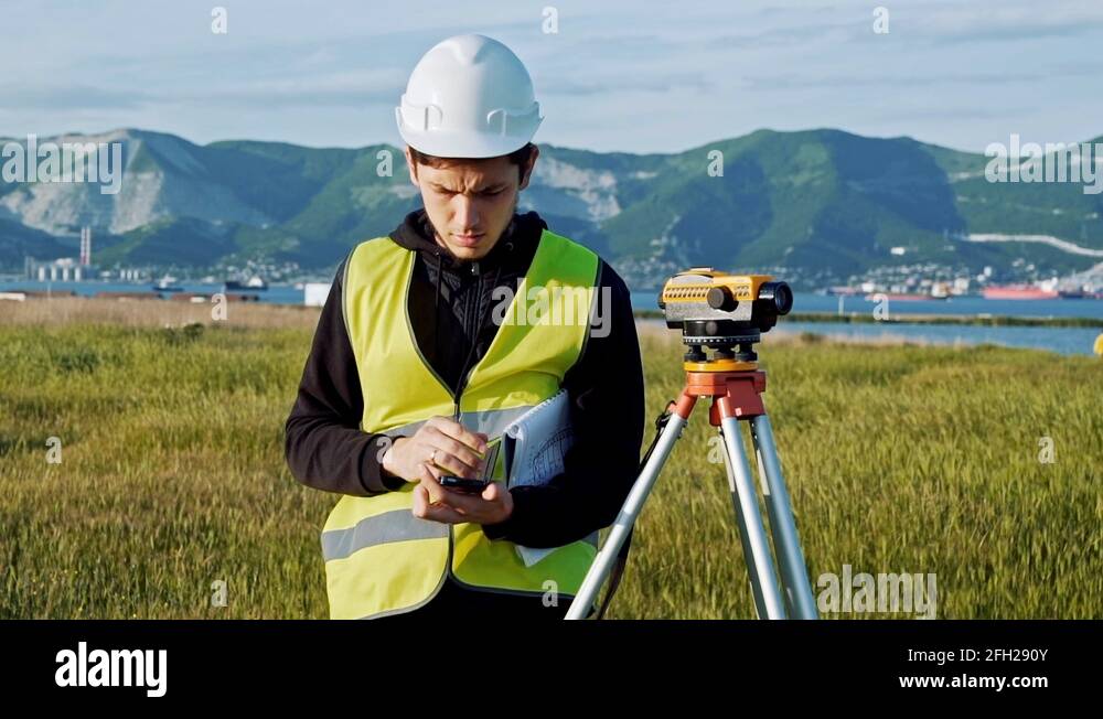 surveyor man in green work clothes and helmet adjusts the equipment ...