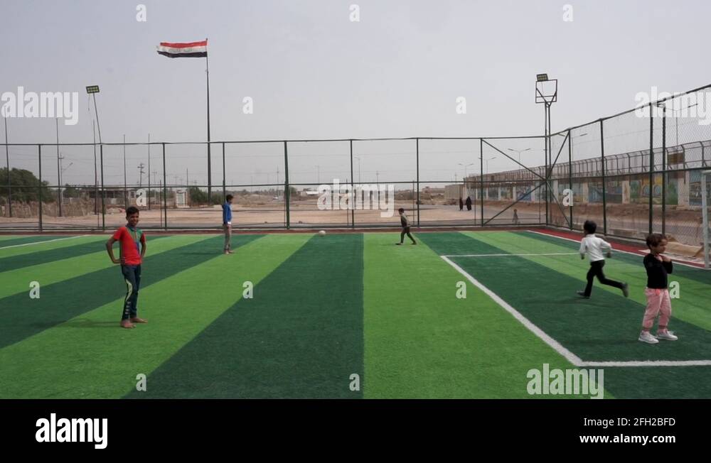 Iraqi children playing on a soccer pitch with an Iraqi flag flying ...
