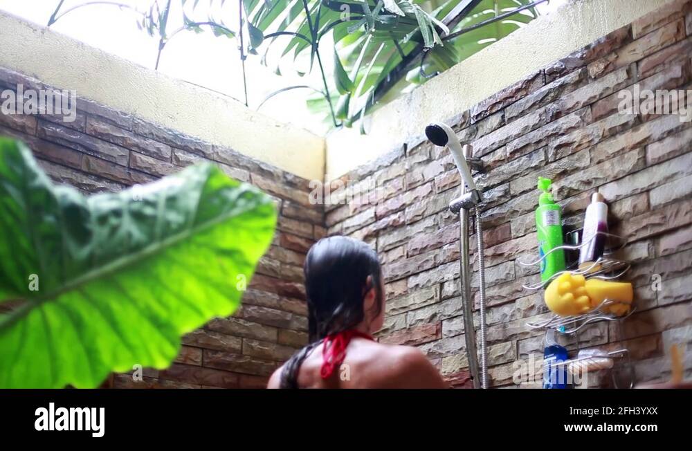 Pretty young woman taking a shower in bikini with flowers in the open ...