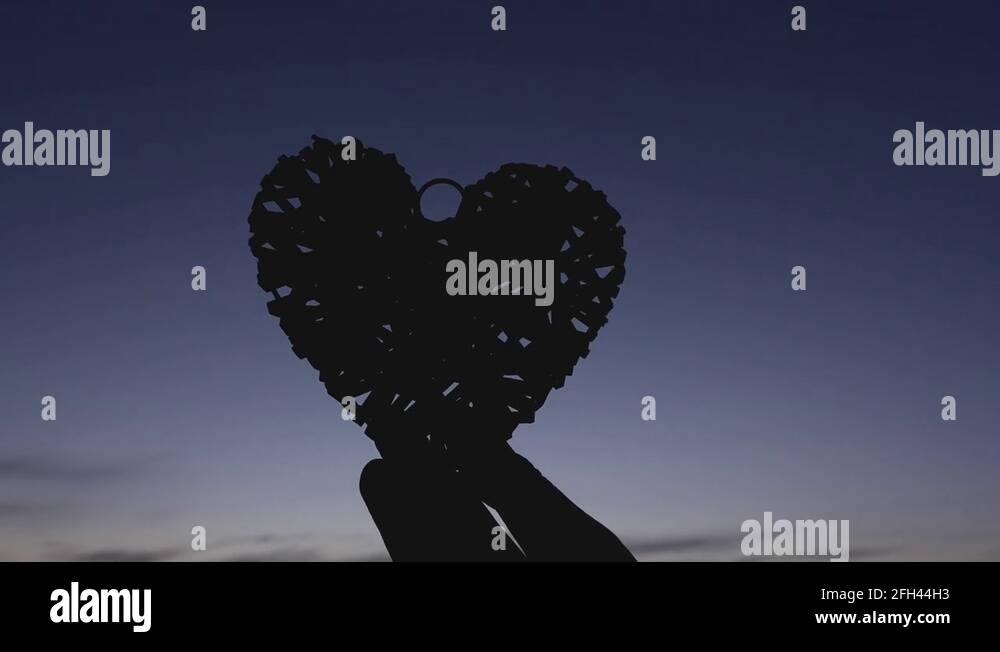 Girl is holding heart in background against cold sunset. Loneliness is ...