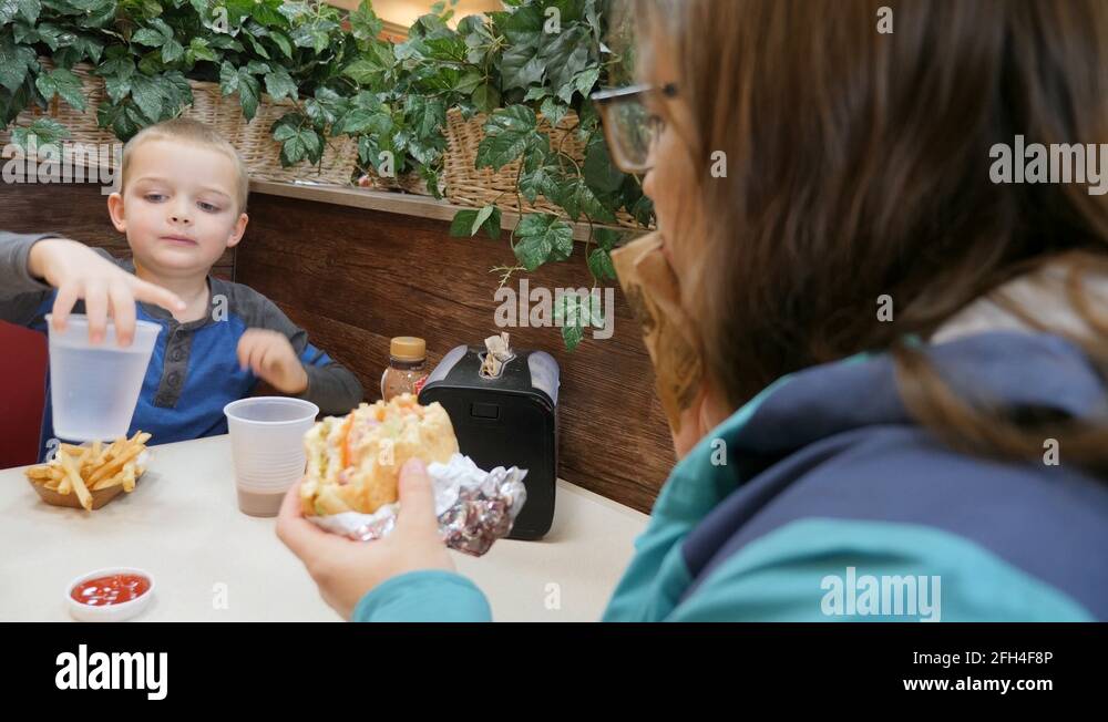 A mother eating large hamburger in fast food restaurant with boy Stock ...