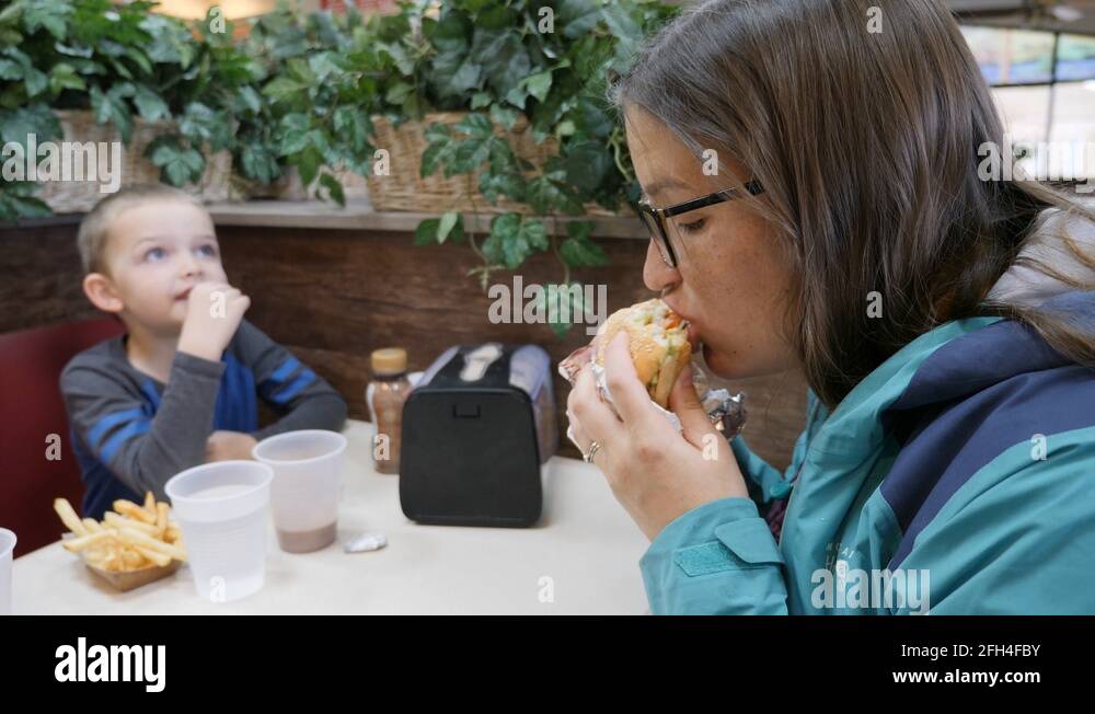 A mother eating large unhealthy hamburger in fast food restaurant Stock ...