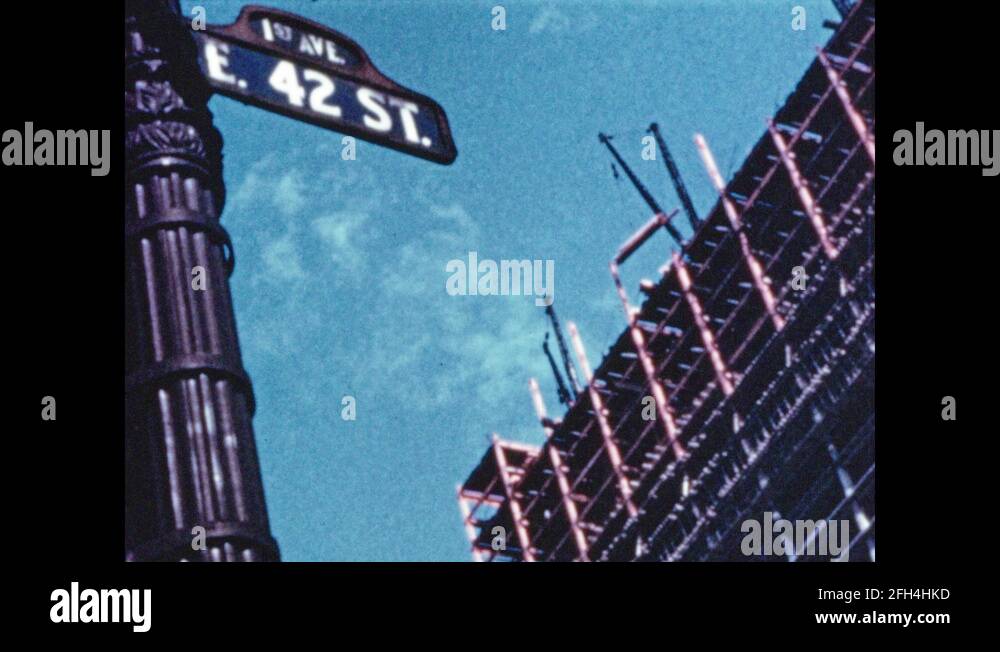 1950s: Skyscraper construction frame and city street sign. Men lower ...