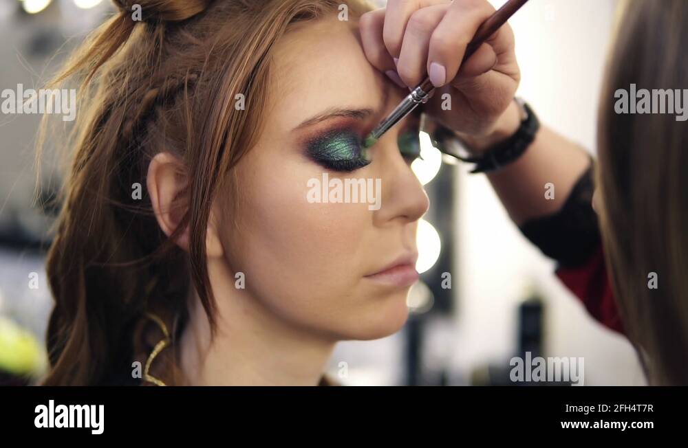 Make-up artist applies some colour shadows on model's eyelids. Side ...