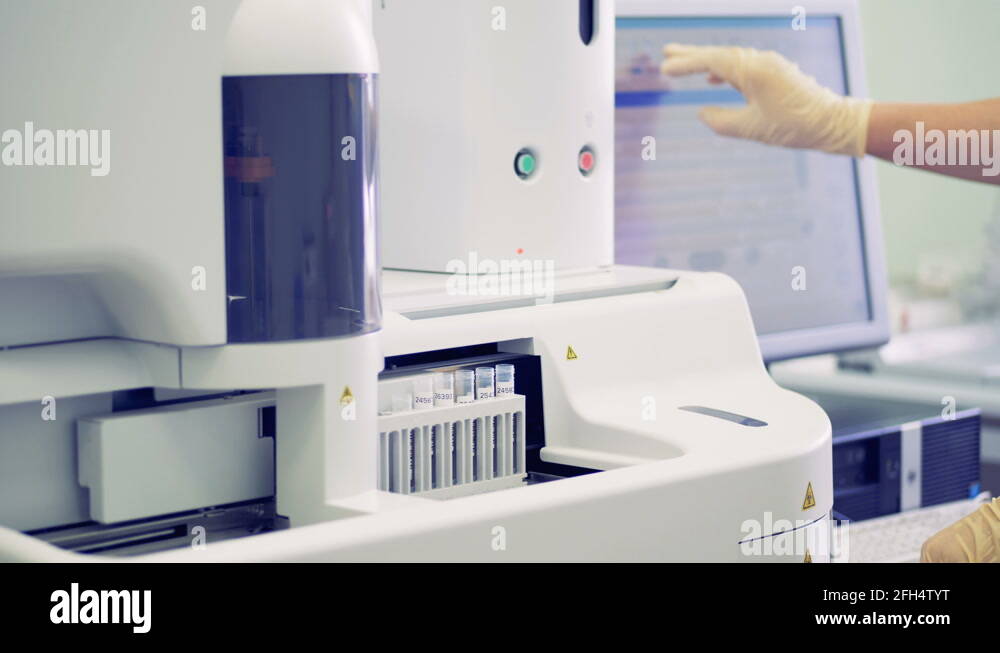 Medical device does a blood analysis, while a nurse types on a monitor ...