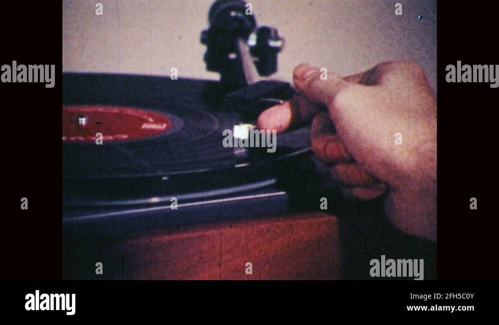 1970s: Hand moves needle on record player and turns dial. Man presses ...