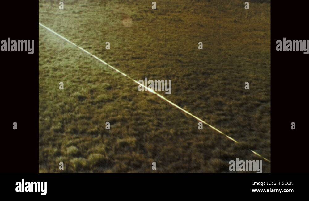 1970s: Aerial view of pipe running through wetlands. Water sprays from ...