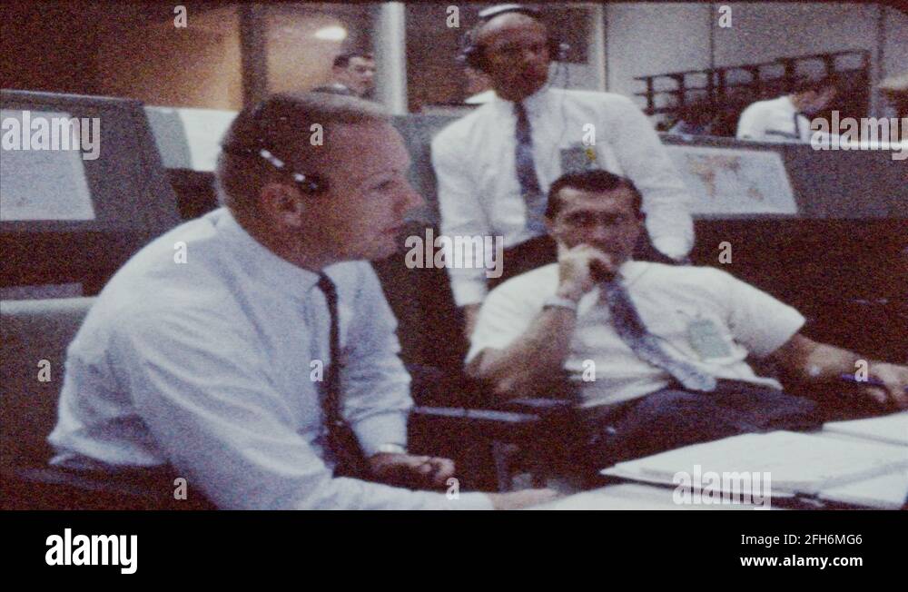 1960s: Men seated at control panel, Neil Armstrong talking, presses ...