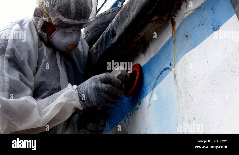 Working people tear off paint on metal in repairs process at shipyard ...