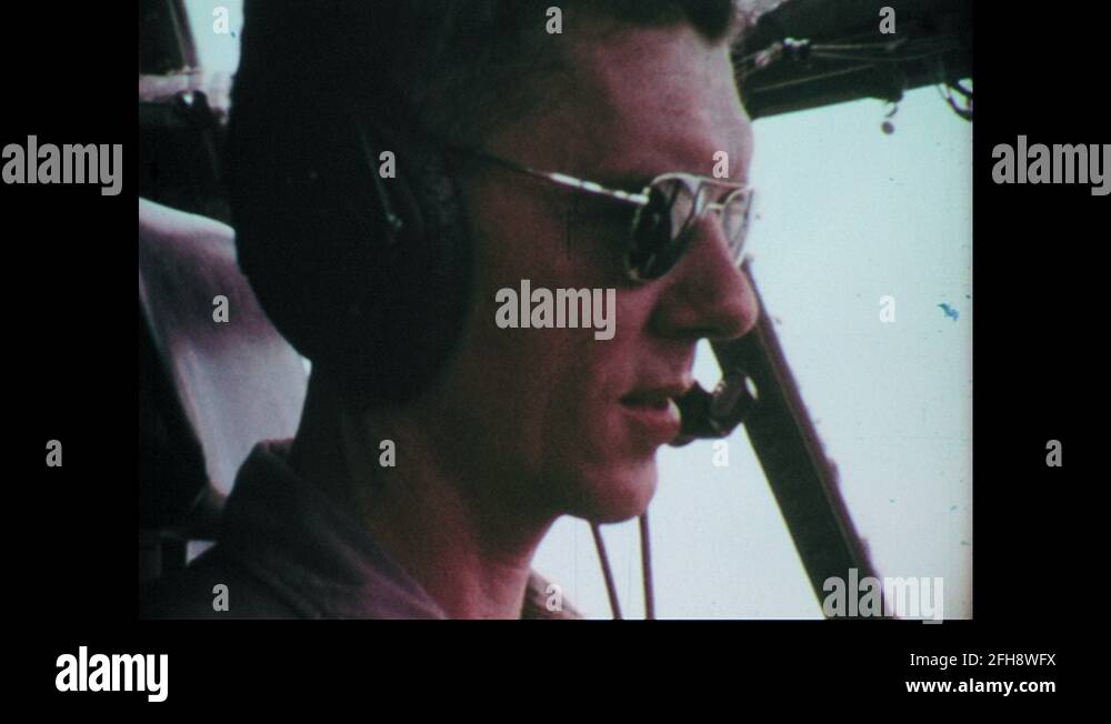 1960s: Pilot wearing headset. Men deploy parachutes and land on ground ...