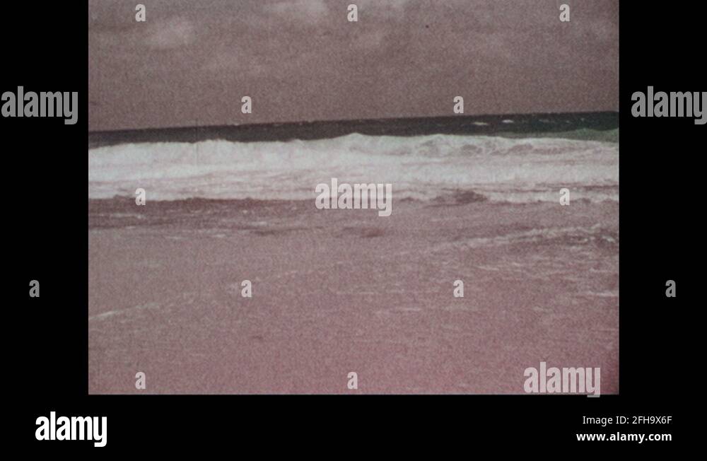 1960s: Waves roll into a beach. Small Mackey Airlines propeller plane ...