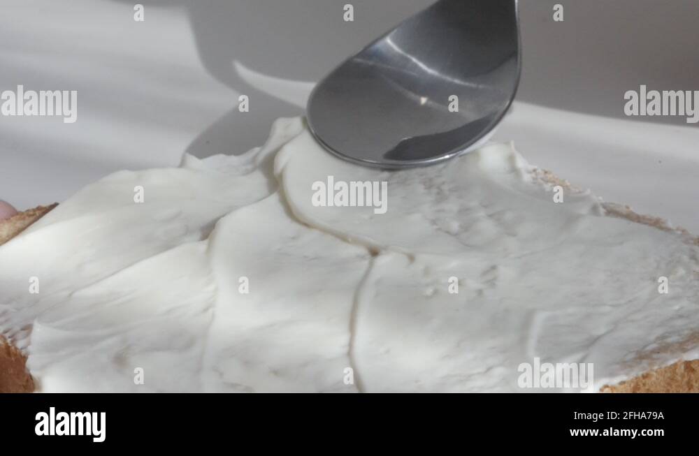 Spoon spreading cream cheese over the bread surface slow motion footage ...