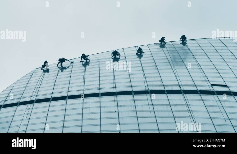 Skyscraper window cleaners. Several window cleaners on top a tall glass ...