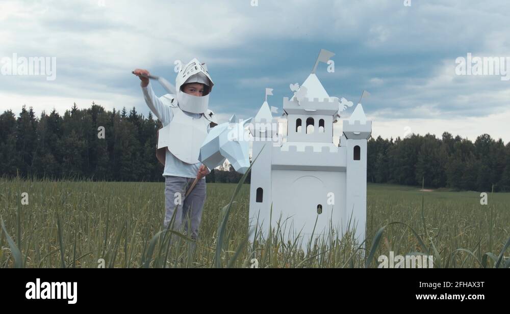 Kid boy wearing cardboard medieval knight armor costume draws a sword ...