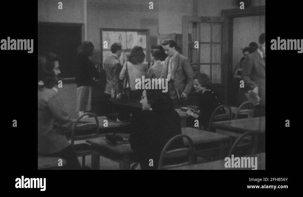1940s: UNITED STATES: students arrive in classroom. Girl sits at desk ...