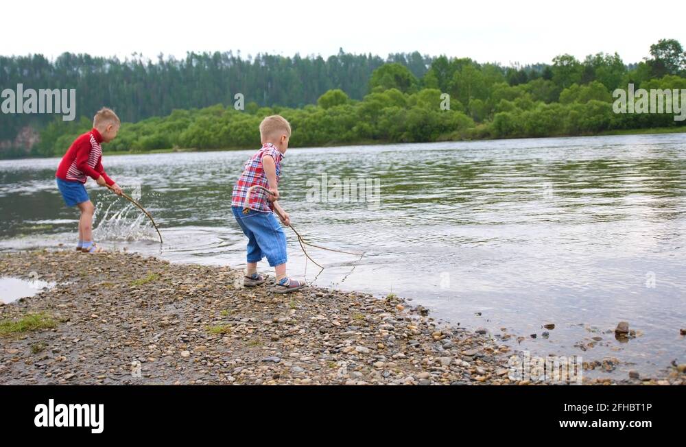 Two children play on the river Bank. Throw stones, make splashes of ...