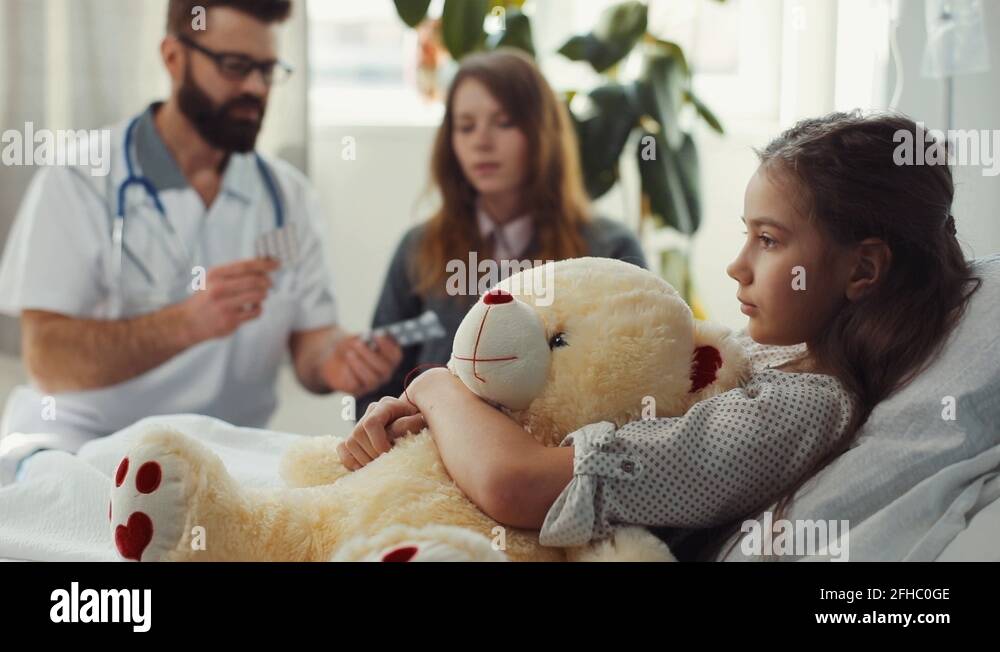 Sick little girl laying on hospital bad, hugging stuffed animal. Mother ...