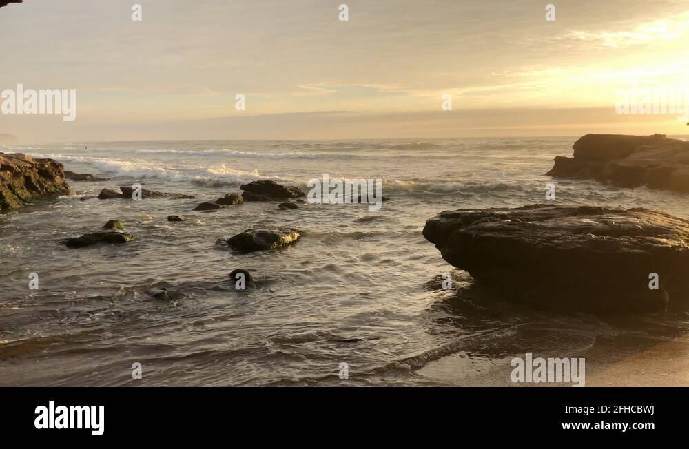 Waves on the beach washing up into a sea cave with the sun low in the ...