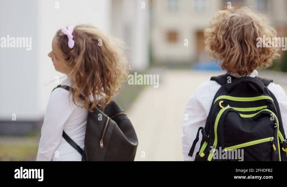Pupils, boy and girl go to school. The children turn around and wave ...