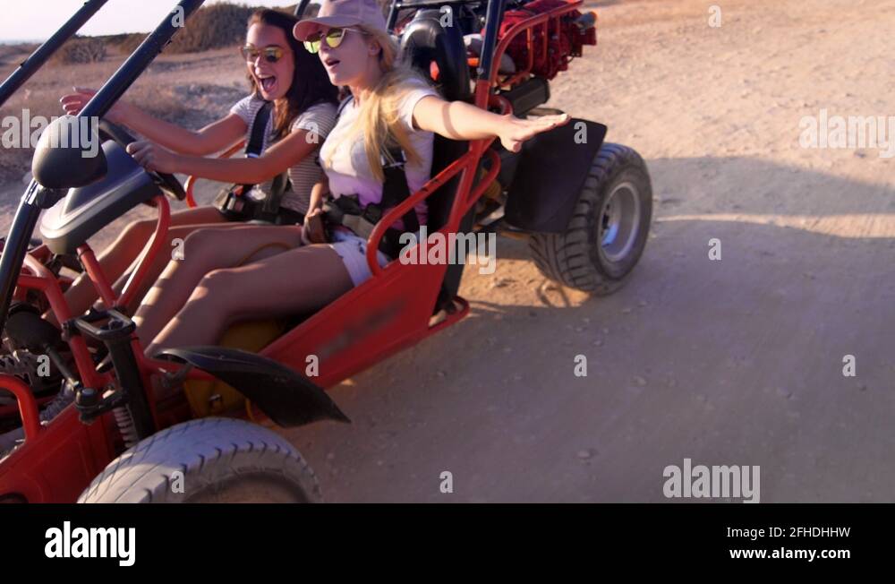 People in dune buggy racing across desert landscape. Girls enjoying ...