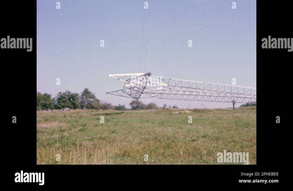 1960s: UNITED STATES: helicopter lifts up structure from ground. Tall ...
